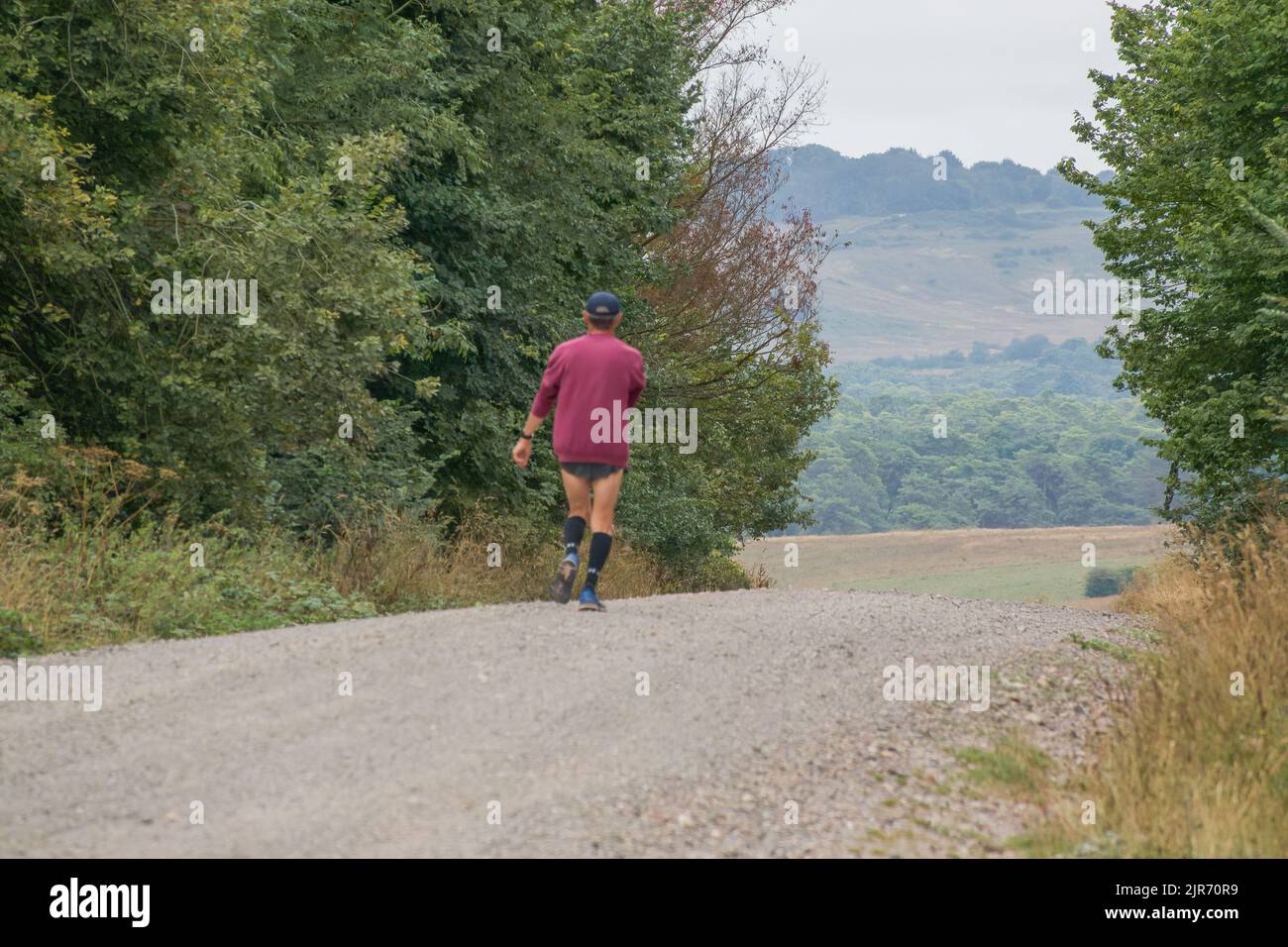 a lone man in a purple top, jogging along an unmade track road, hiking ...