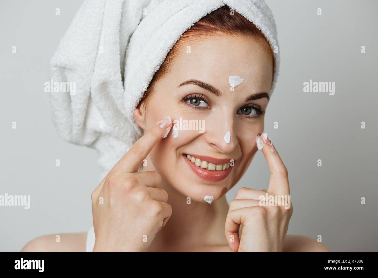 Portrait Of Caucasian Young Lady Applying Face Cream Over Grey