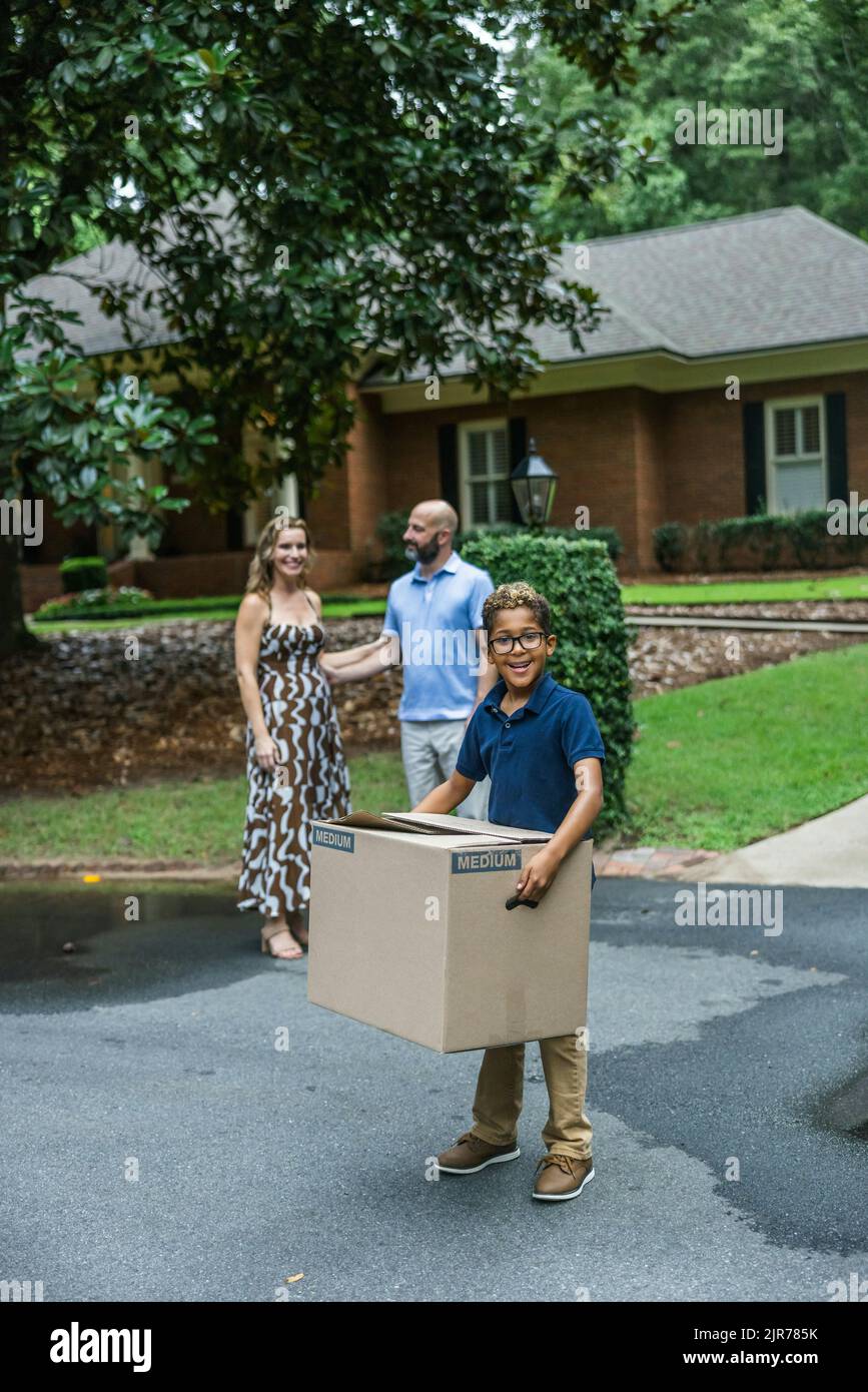A little boy holding a moving box ready to move into his new house ...