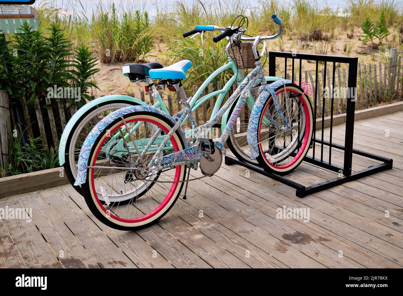 Two colorful bicycles stand parked on a boardwalk bicycle rack near ...