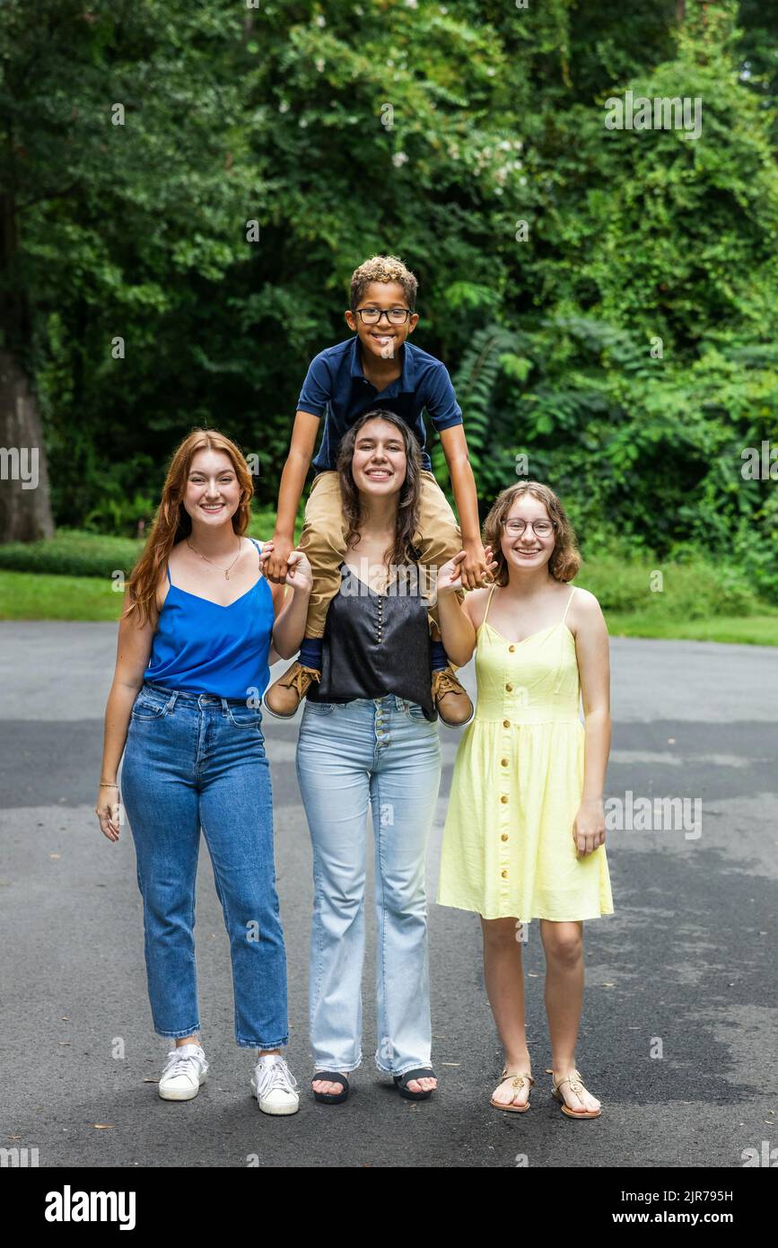 Four siblings with the youngest one sitting on his big sister's ...