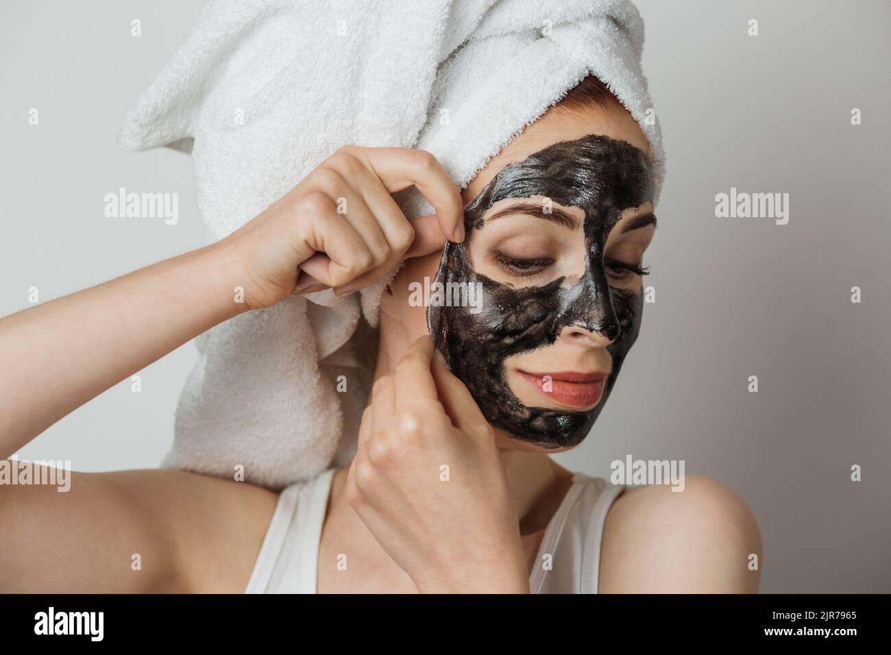 Beautiful young woman removing black cosmetic mask from face in white ...