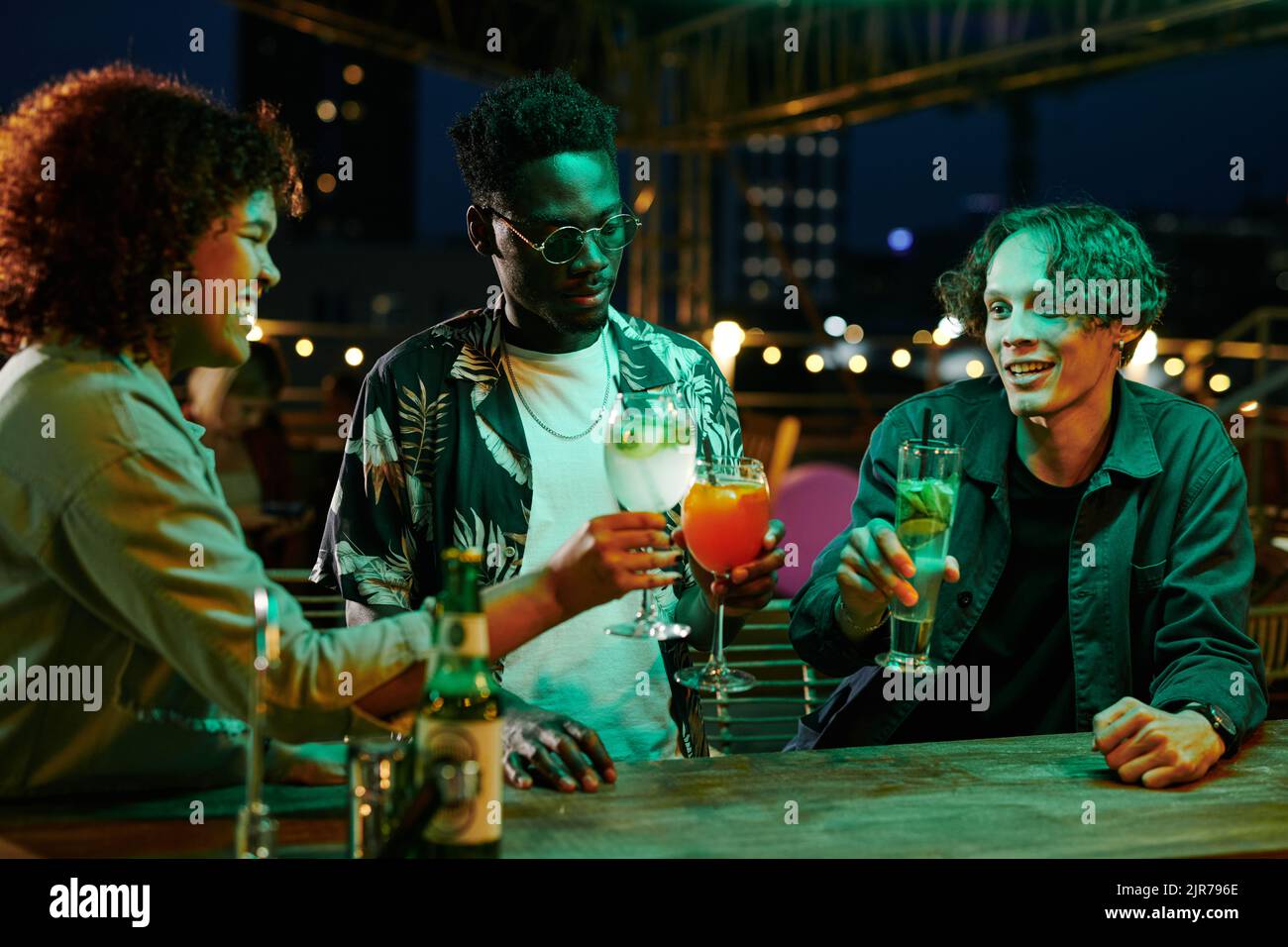 Three young multicultural friends in casualwear toasting with cocktails ...