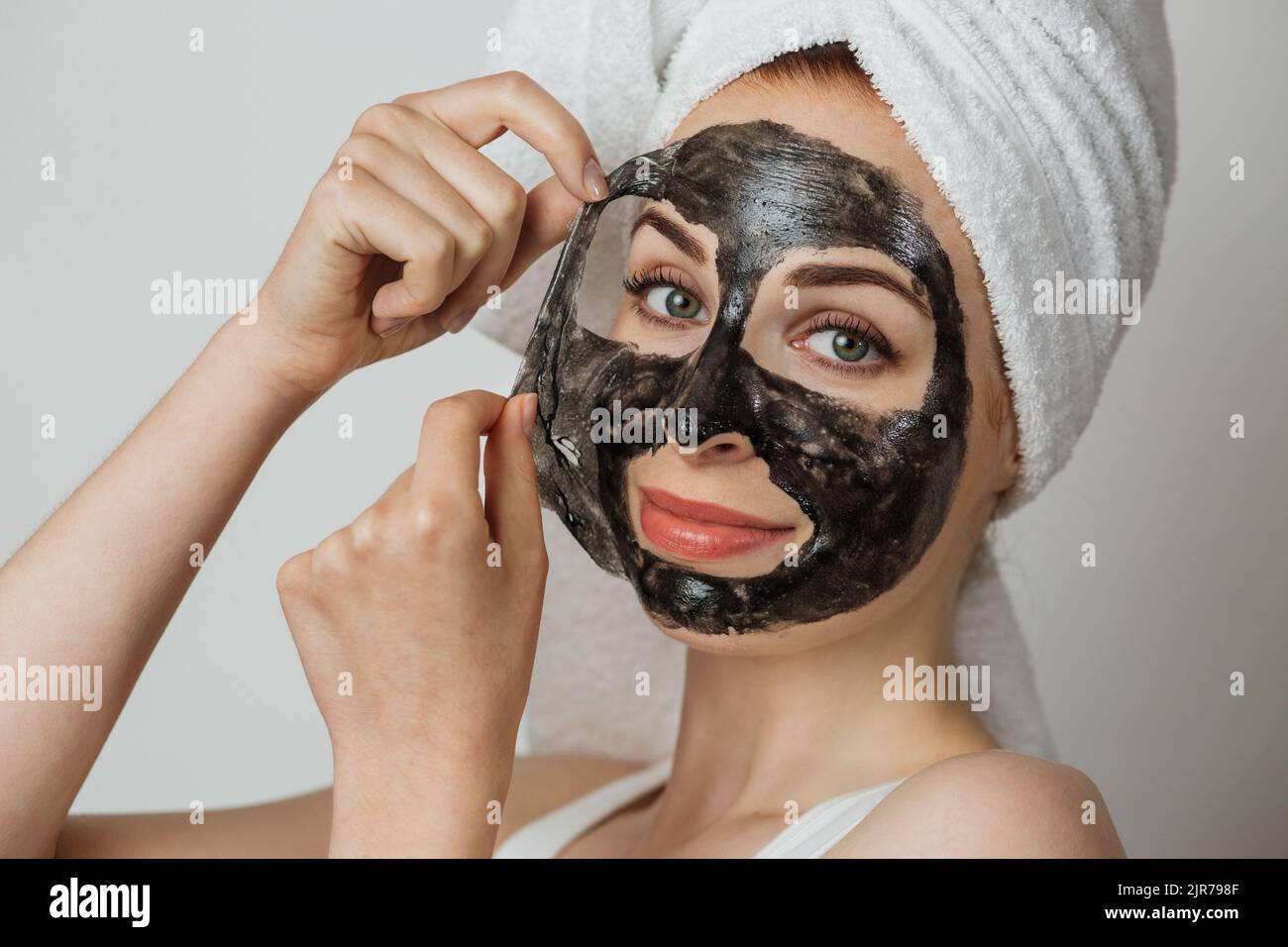 Portrait of smiling young woman n towel removing cosmetic mask from ...