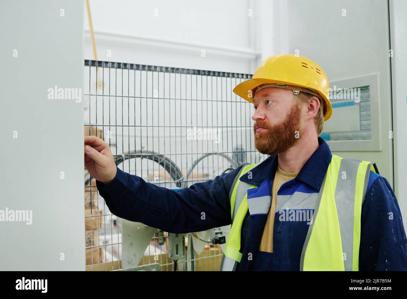 Serious male technician or engineer pressing start button to switch on ...