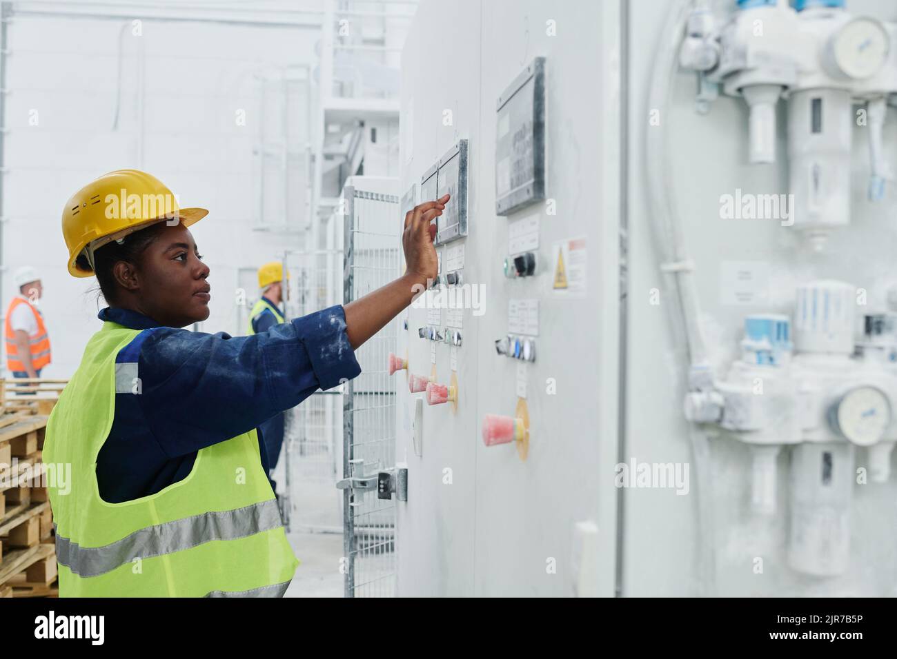 Young African American woman in uniform and hardhat pressing button on ...