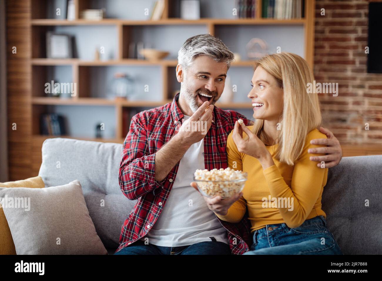 Smiling adult caucasian wife and husband eating popcorn, watching tv ...