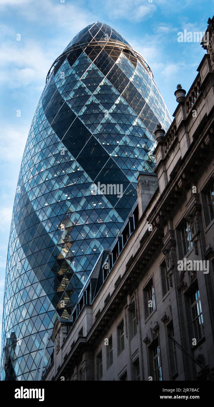 A vertical shot of The Gherkin skyscraper in daylight with blue cloudy ...