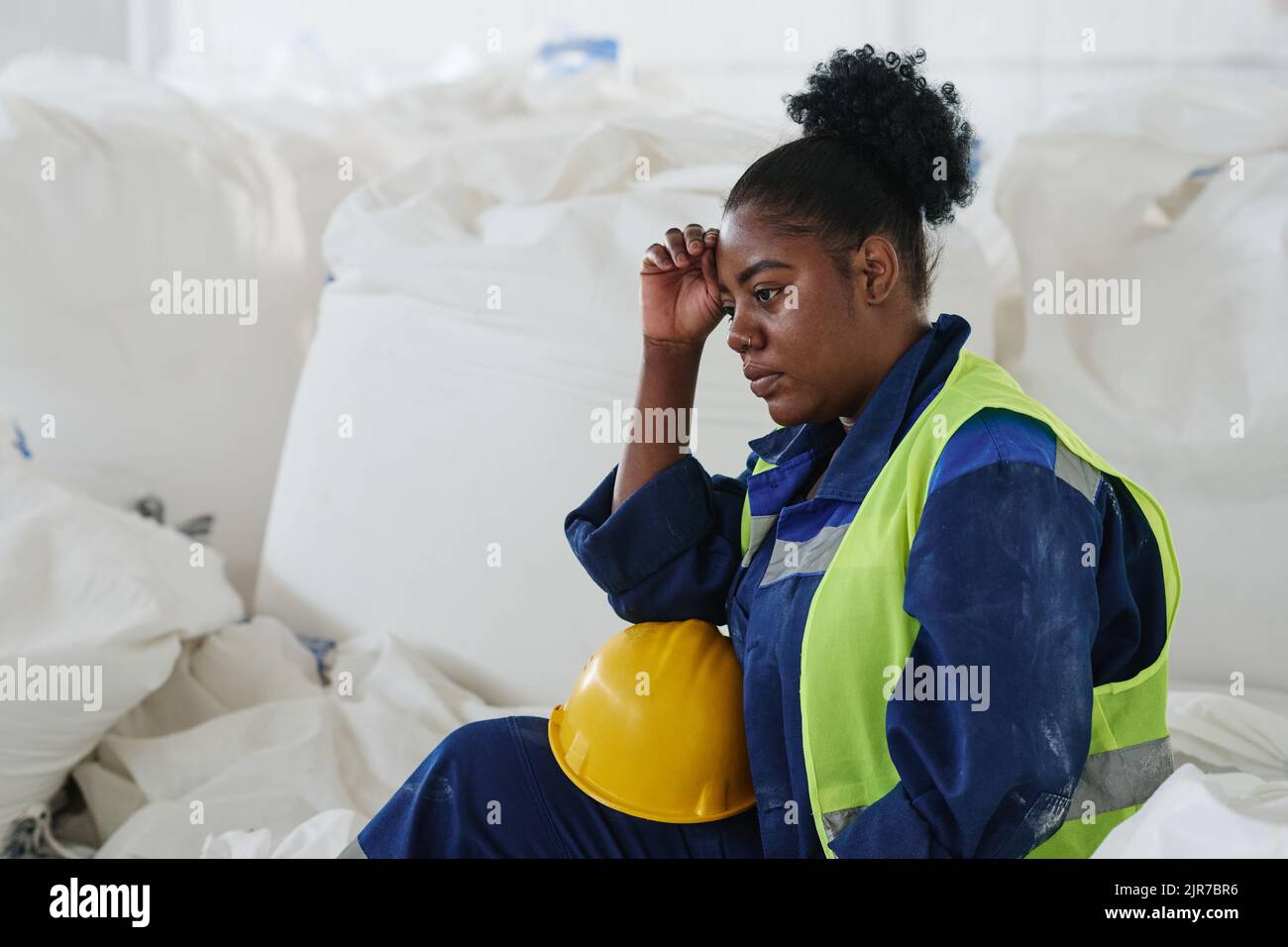 Young tired female engineer or worker of warehouse sitting by heap of ...