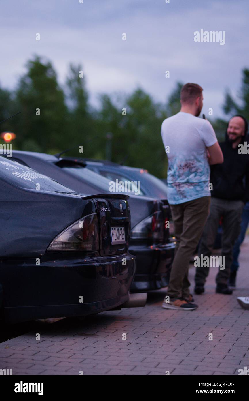 A vertical view of cool men standing behind parked modern cars in ...