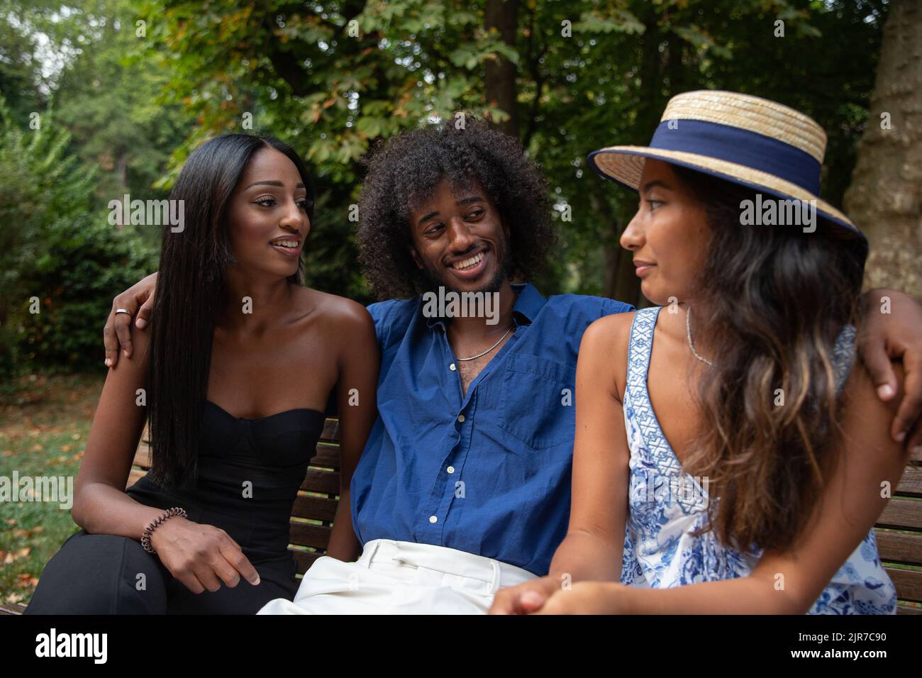 Group of three friends sitting on the bench at the park talking to each ...