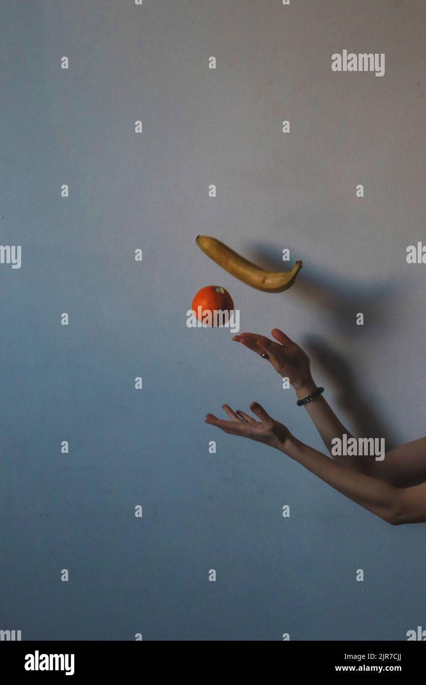 Female hands throwing a orange and a banana in the air, blue background ...