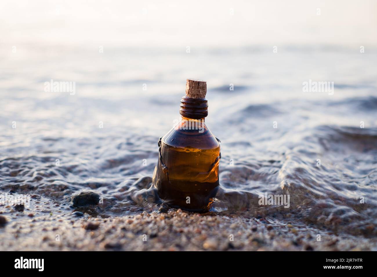 Essential oil bottle on a beach in waves. Little brown medicine bottle ...
