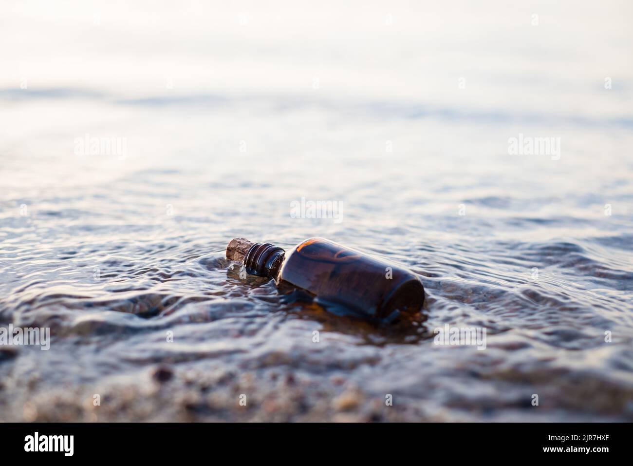 Essential oil bottle on a beach in waves. Little brown medicine bottle ...