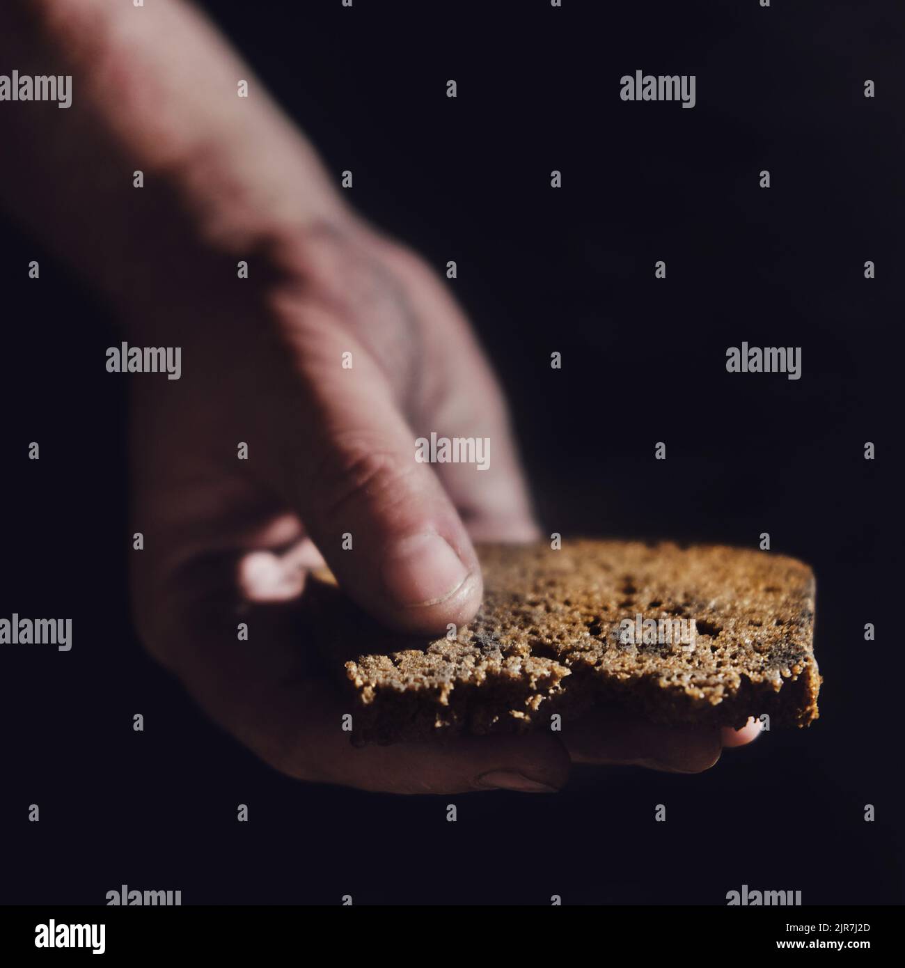 Hungry man holding bread on a black background, hands with food close ...