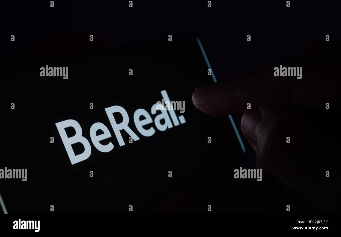 Finger touching blurred Bereal app logo in the dark. BeReal is a new ...