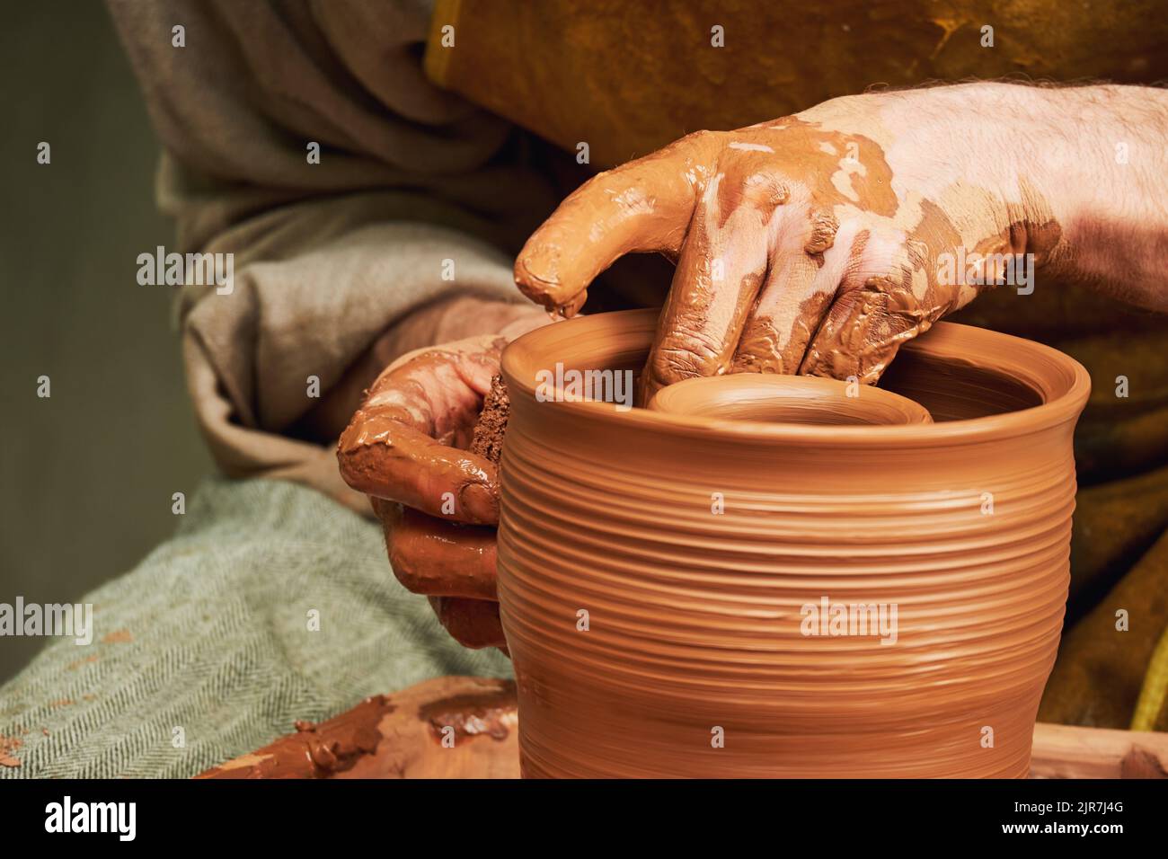 A man in old medieval Byzantine clothes sits behind a vintage potter's ...