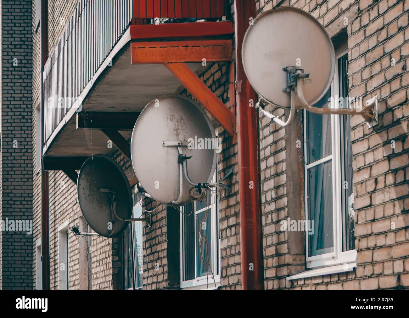 old satellite dishes hang on the wall of an old house near the windows ...