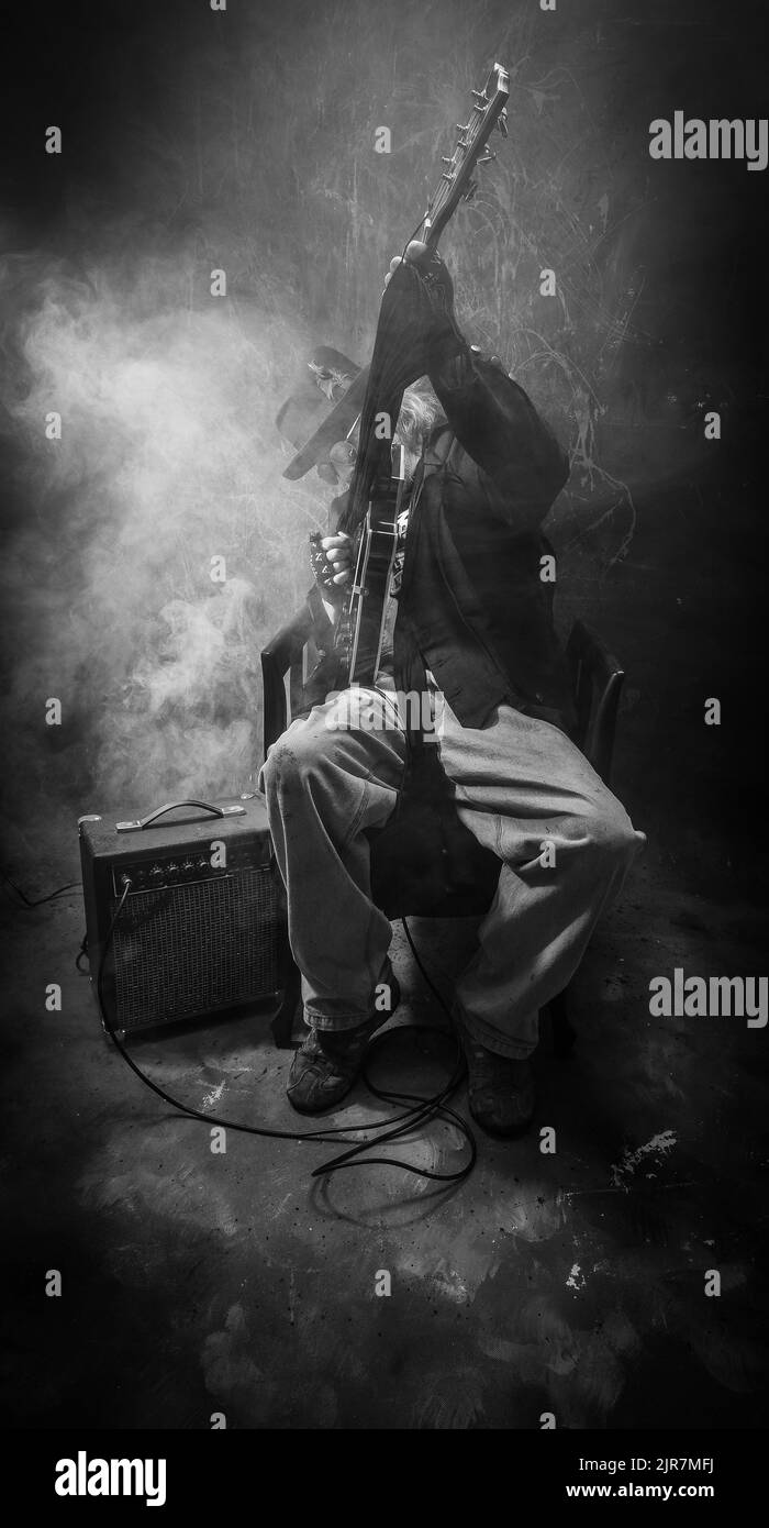 A Vertical Grayscale Shot Of An Old Guitarist Sitting In The Dark