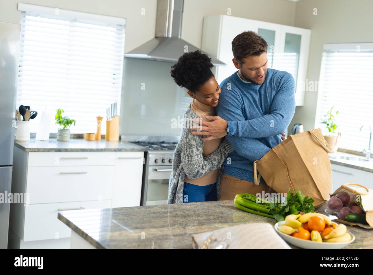 Image of happy diverse couple embracing and unpacking groceries in ...