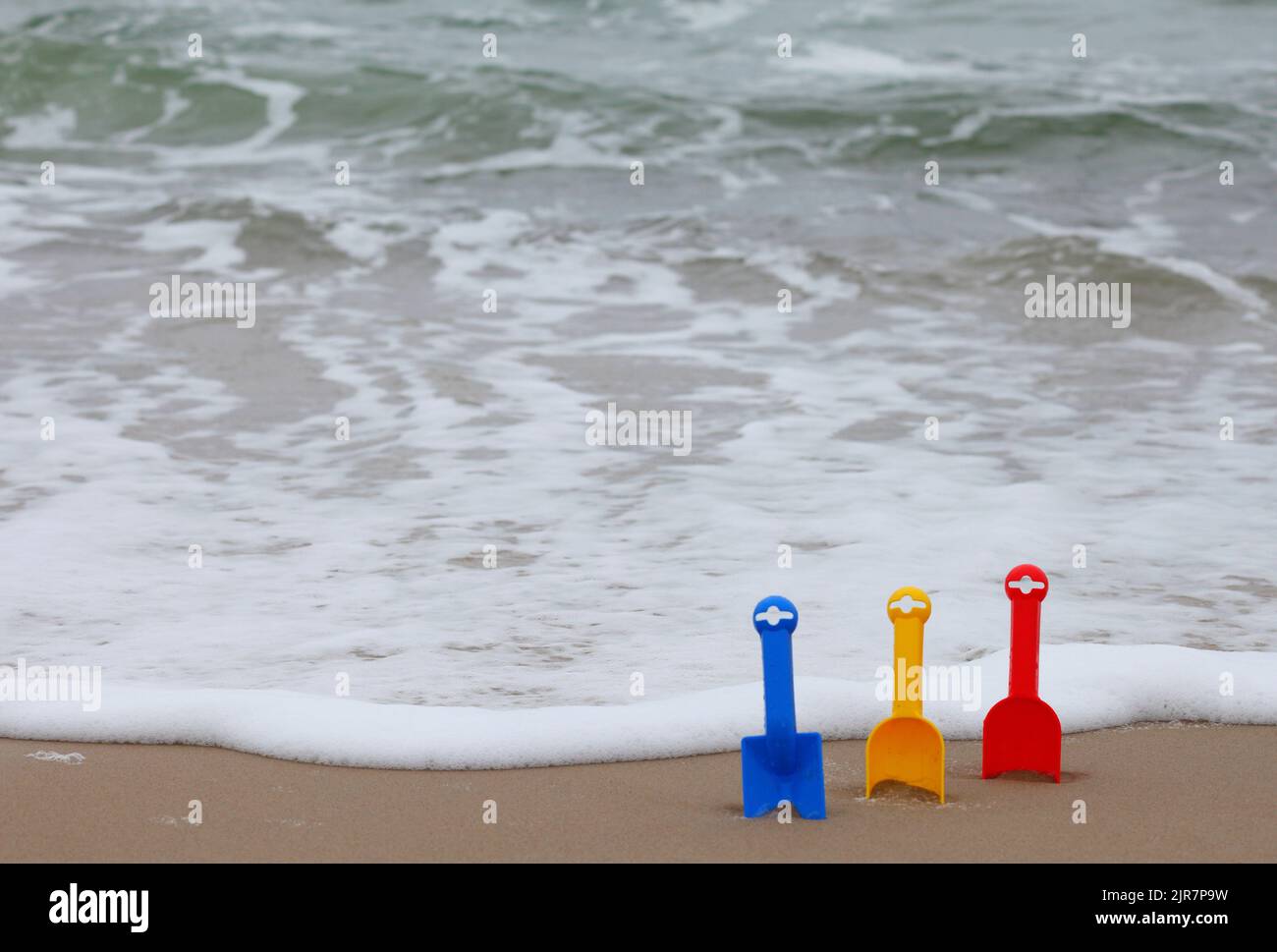 Three colorful shovels in the beach sand with the ocean waves in the ...