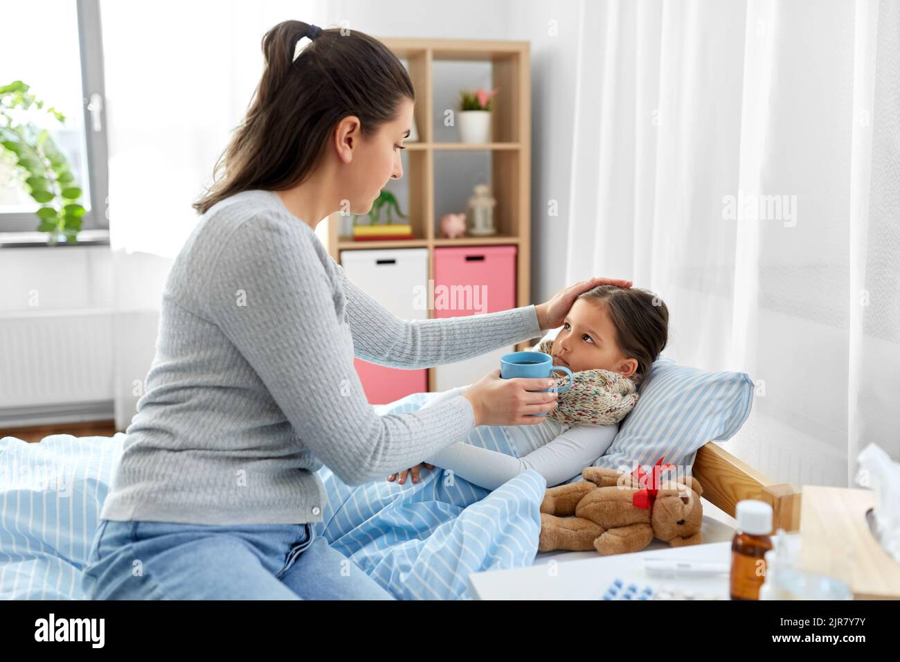 mother giving tea to sick daughter lying in bed Stock Photo - Alamy