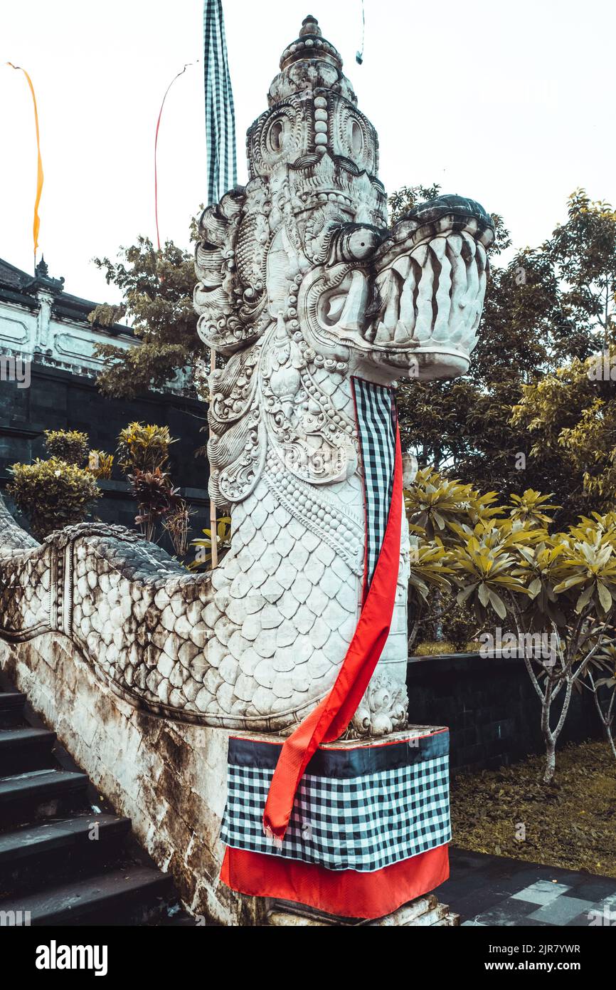 A vertical shot of One of the many amazing statues in Bali on the fence ...