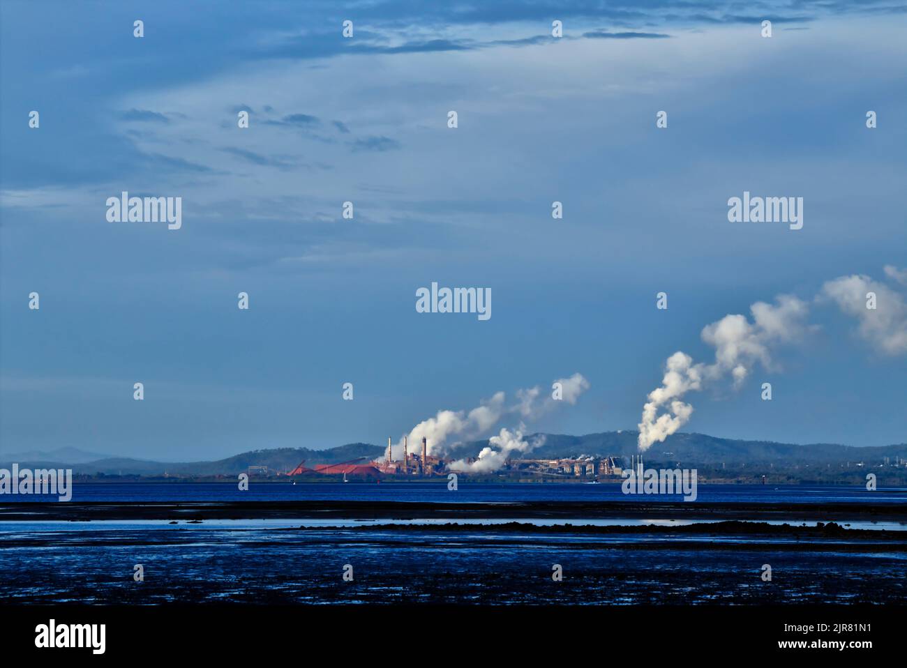 Industrial landscape with smokestacks emitting smoke over a coastal ...