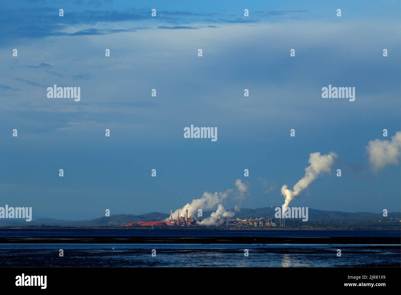 Industrial landscape with smokestacks emitting smoke over a coastal ...