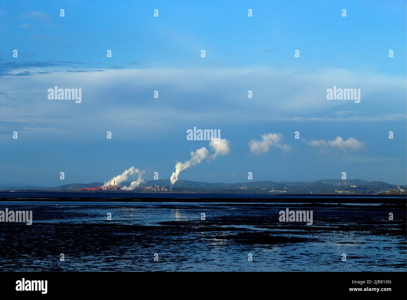 Industrial landscape with smokestacks emitting smoke over a coastal ...