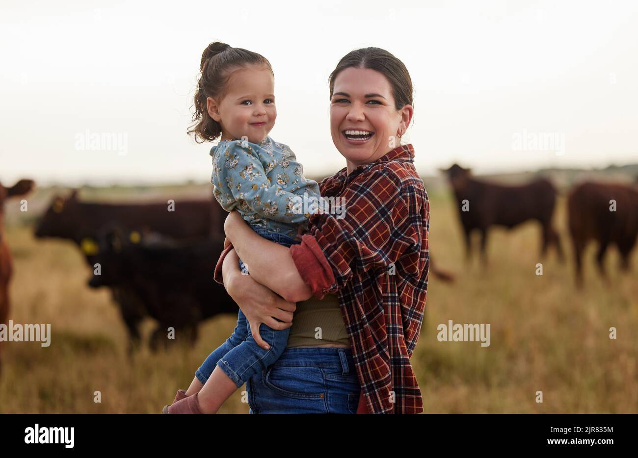 Family, mother and baby on a farm with cows in the background eating ...