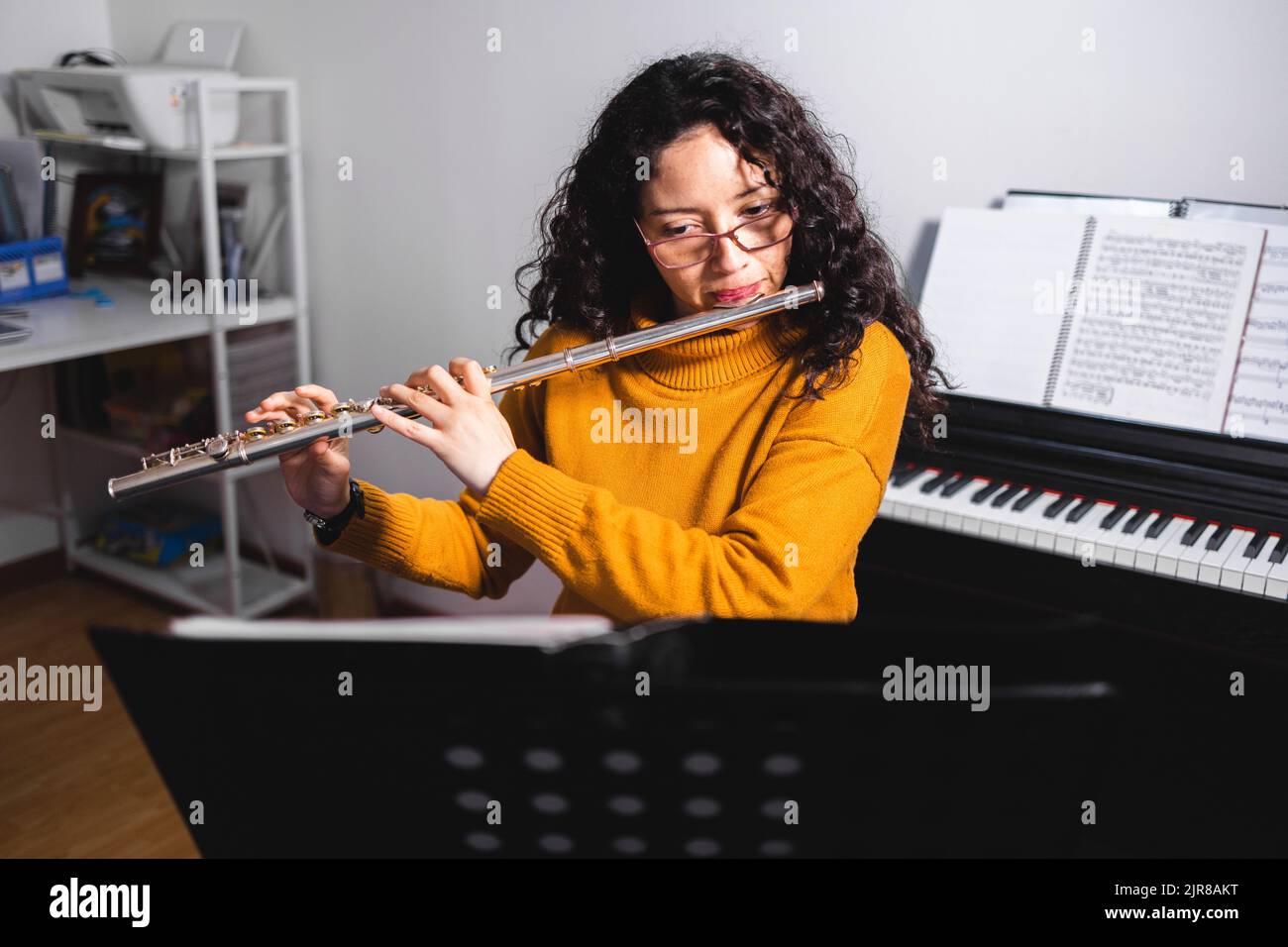 Brunette woman wearing a yellow sweater, and playing a transverse flute ...