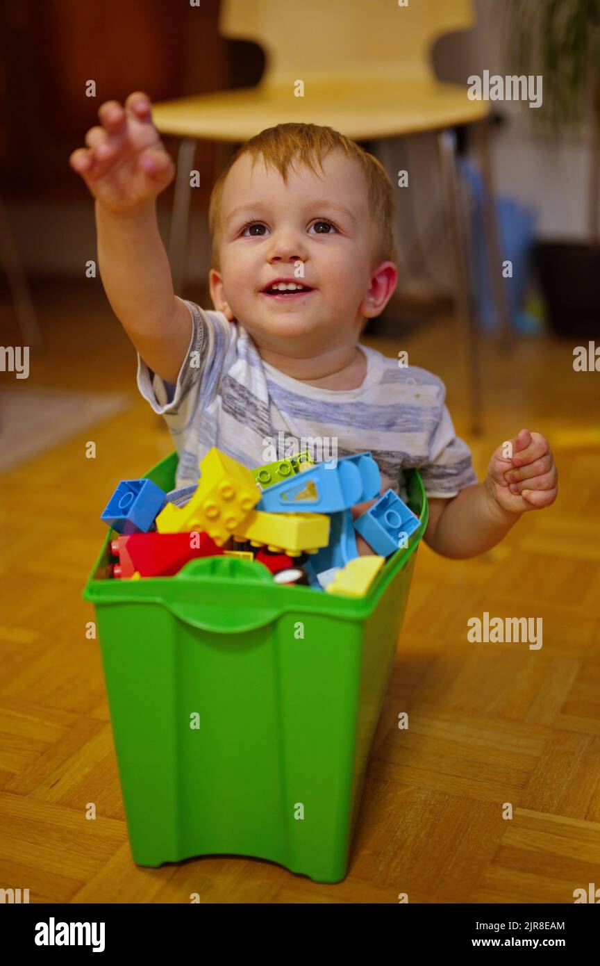 Cute little boy sitting in the plastic box and playing with blocks set ...