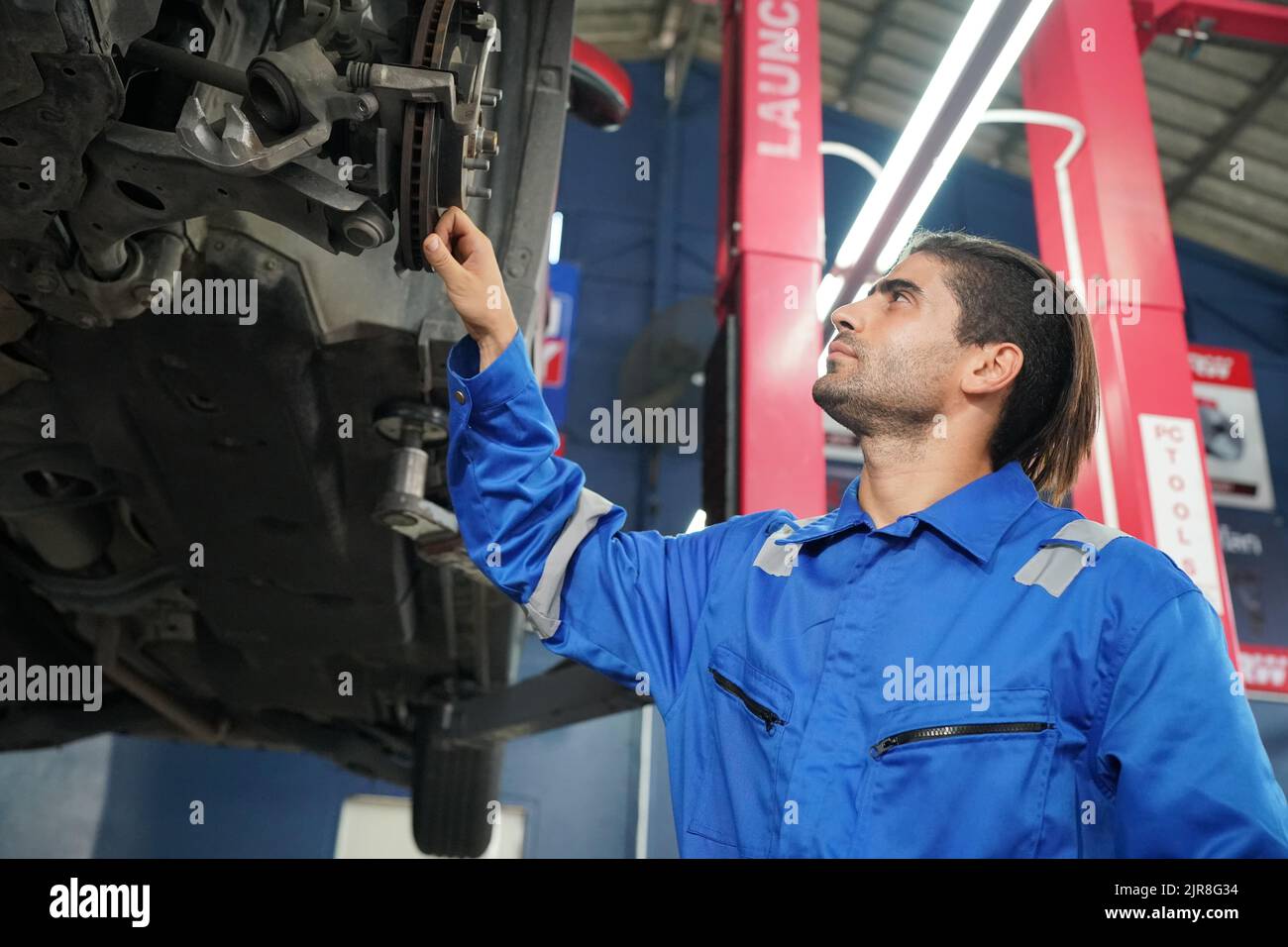 Male car operator wearing blue overalls,cap and gloves working under ...