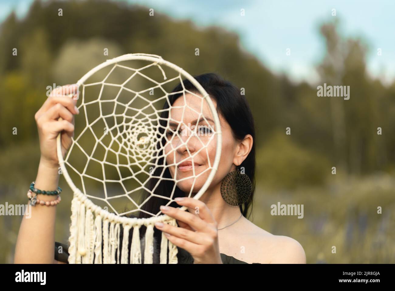 An attractive woman in a summer field with a dream catcher. Front view ...