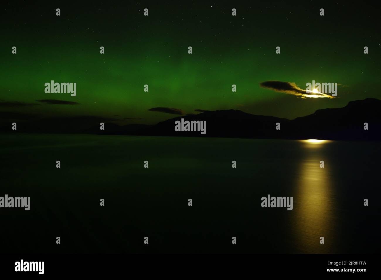 The aurora borealis shines with a rising moon over the waters of Alaska ...