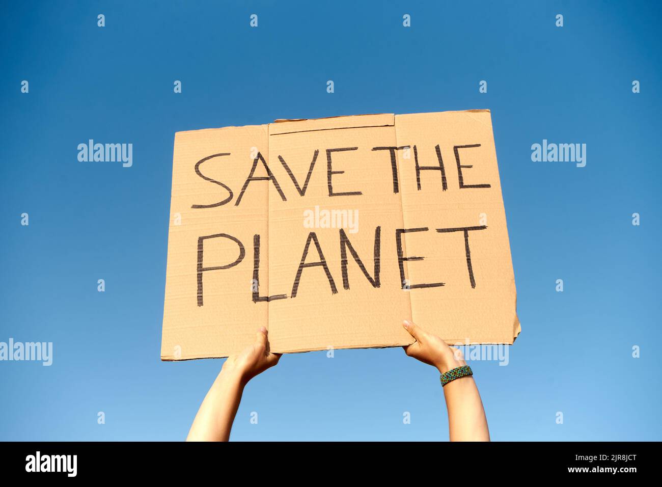 A cardboard sign saying Save the Planet held by two hands on a clear ...
