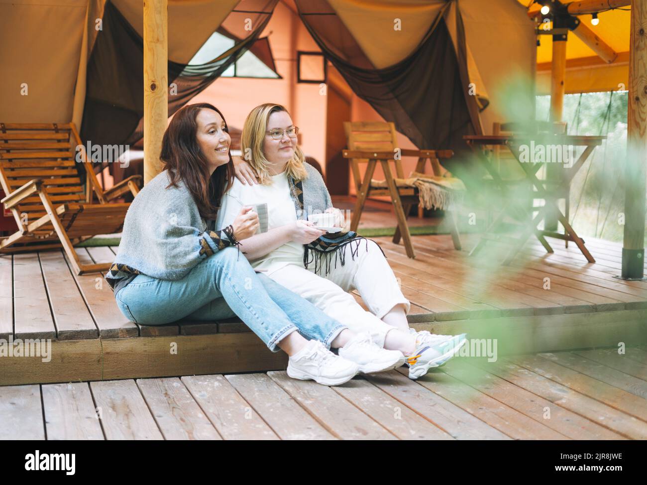 Two young women friends drinking tea and relaxing in glamping in the ...