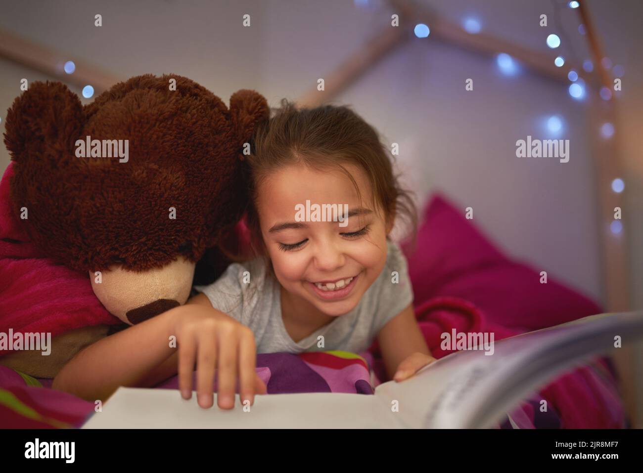 Teddy loves reading along with her. a little girl reading a book in bed ...