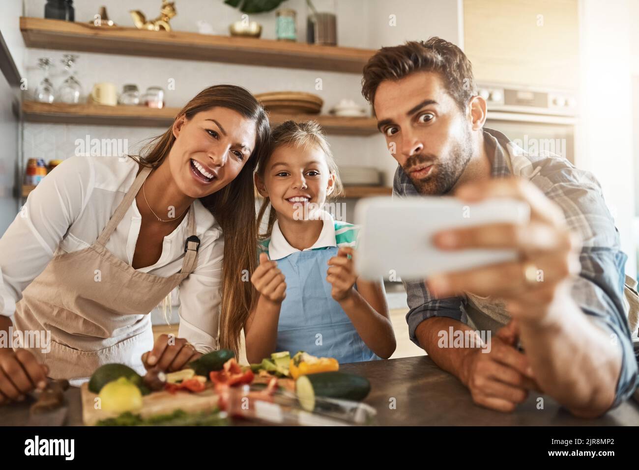 Funny faces in the kitchen. a happy young family posing for a selfie ...