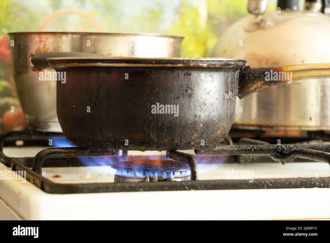 a dirty saucepan stands on a dirty gas stove in the kitchen at home ...
