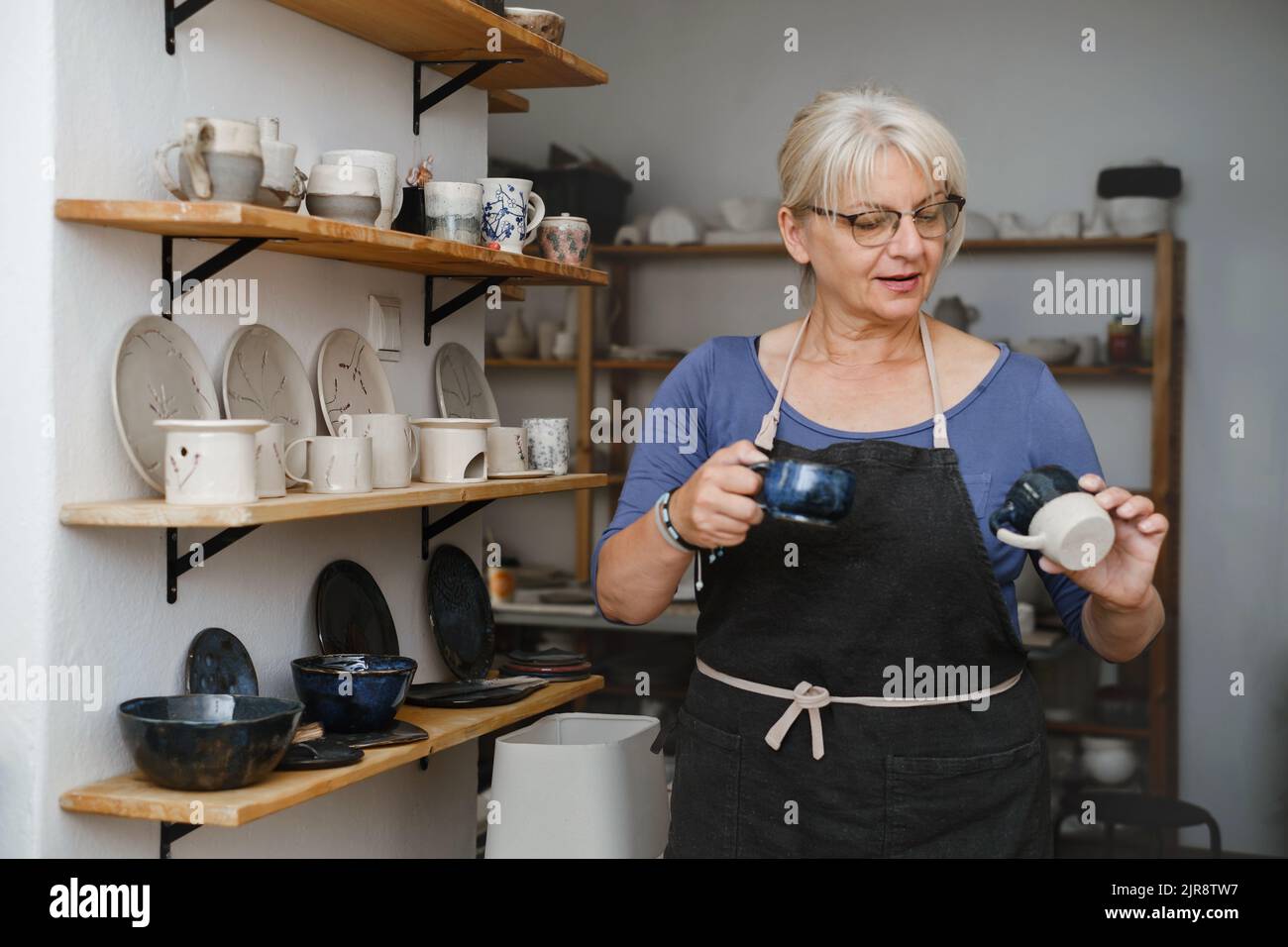 Potter artist showing her work in studio. Mature ceramist standing at ...