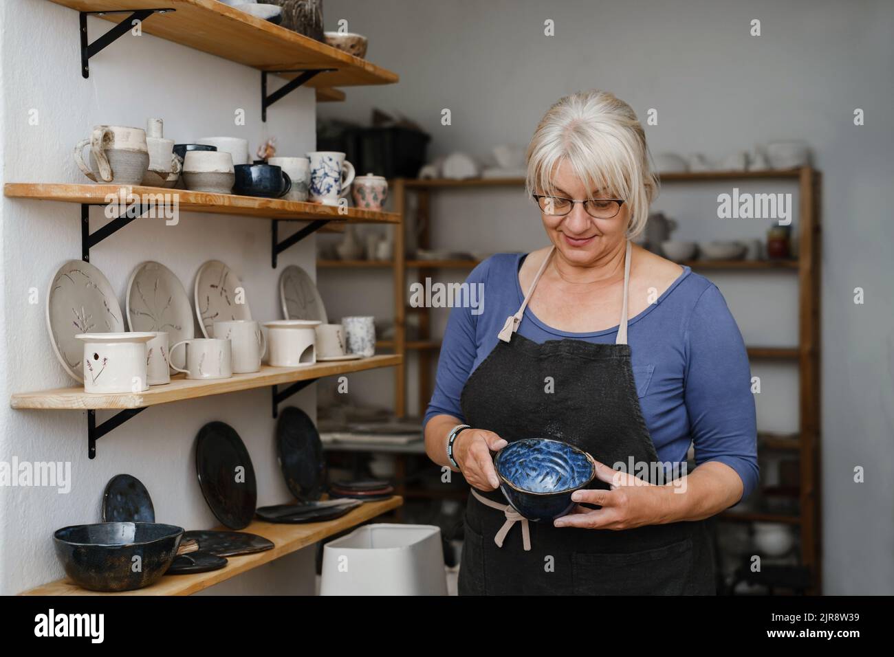 Potter artist showing her work in studio. Mature ceramist standing at ...