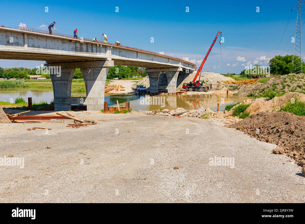 Team of workers are working on the unfinished bridge, road over river ...