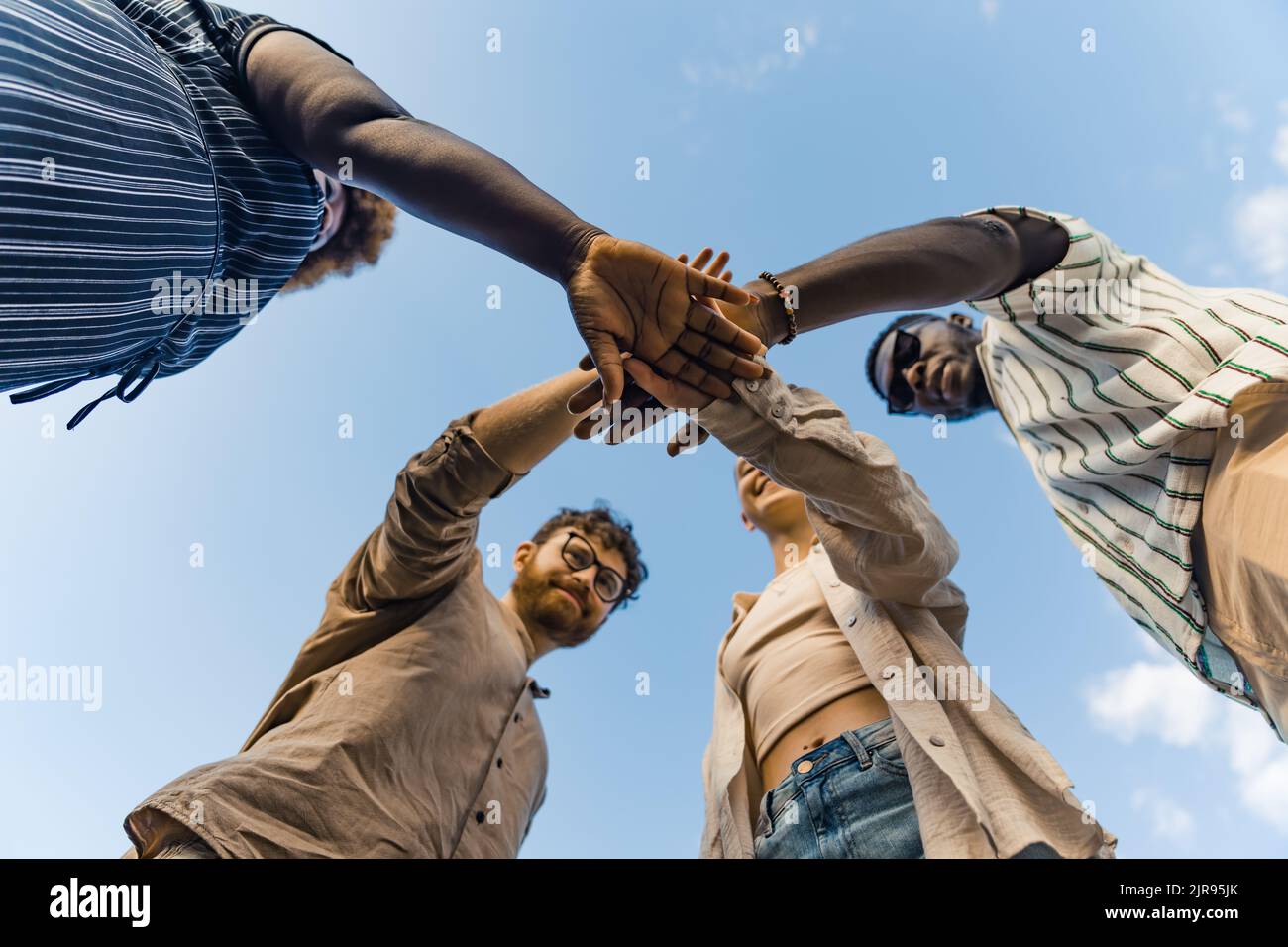 Multicultural group of young people standing in circle and holding ...