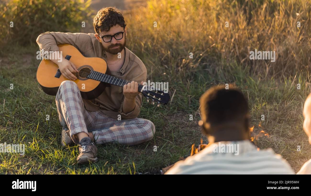A young bearded caucasian man playing the guitar during a picnic in ...