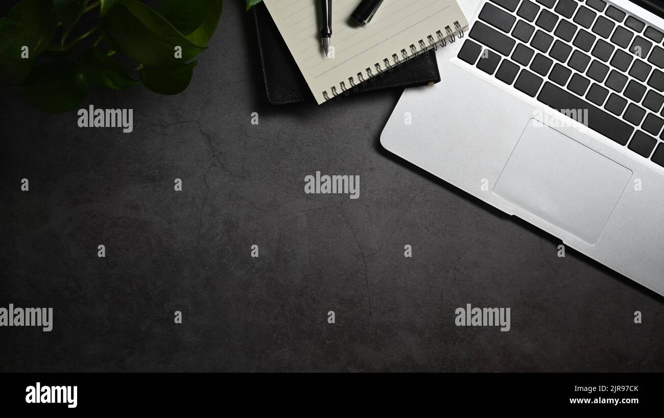 Top view laptop computer, notepad and pen on dark stone background with ...