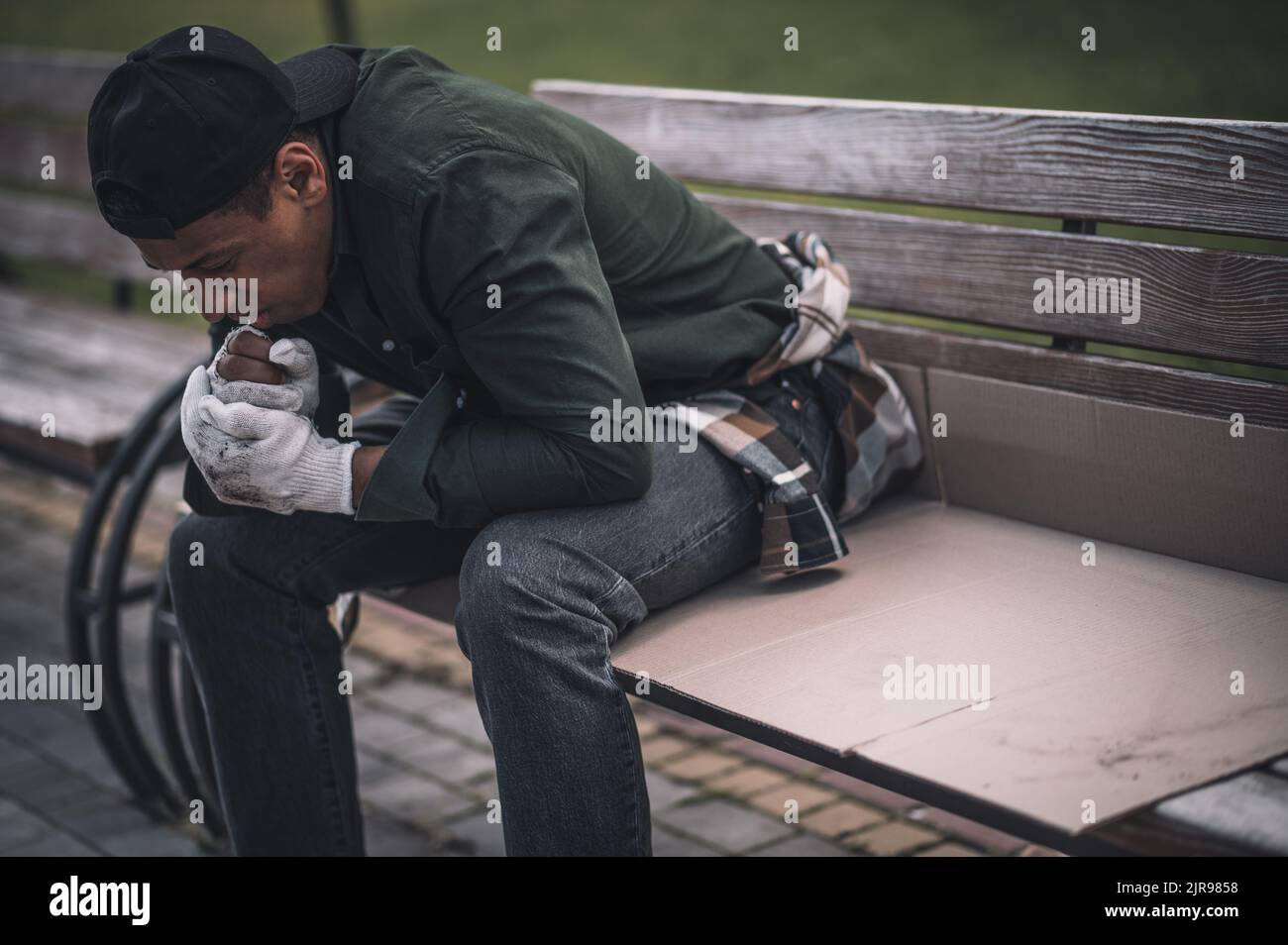 Man sitting crouched on bench in park Stock Photo - Alamy
