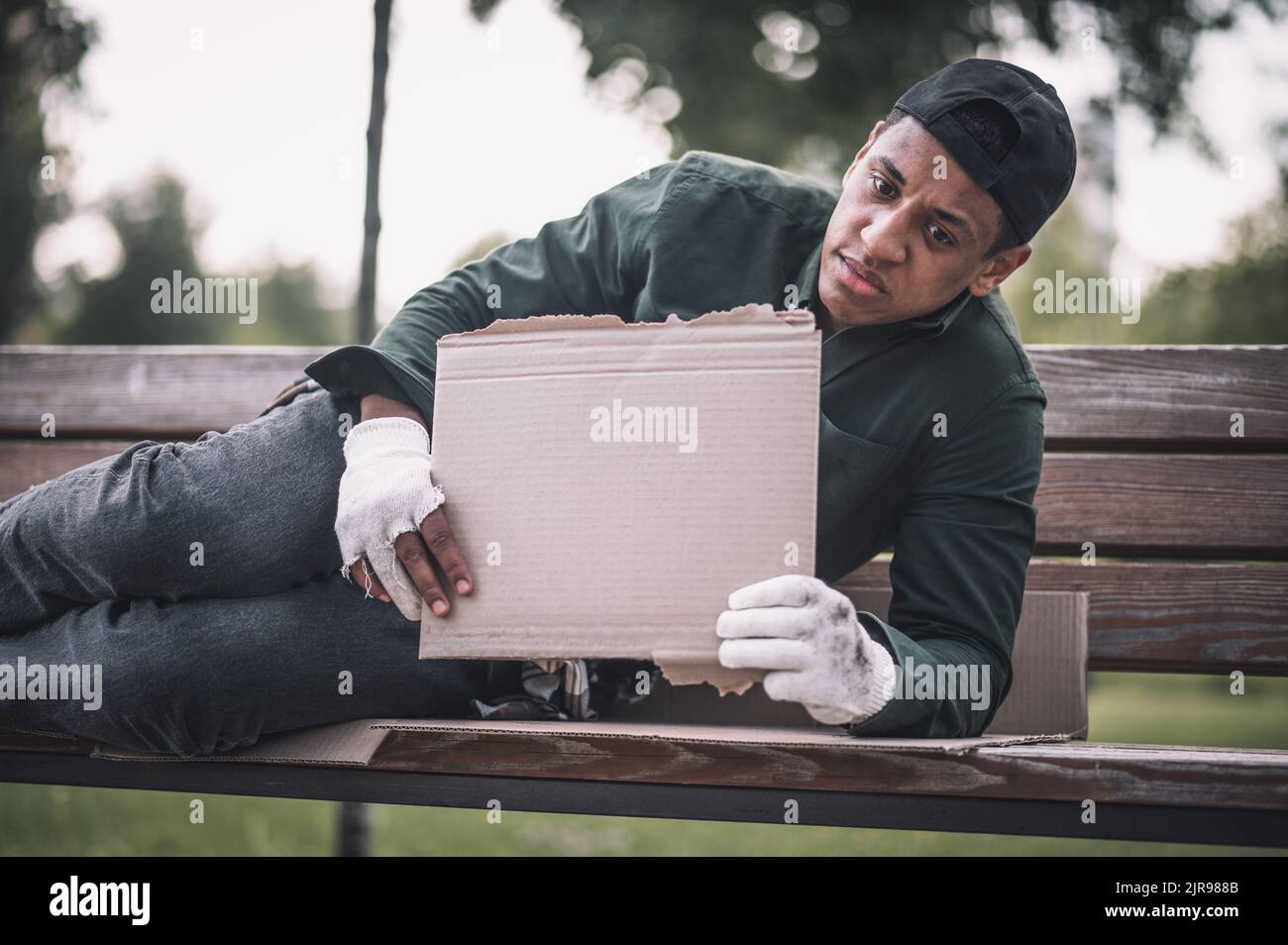 Man reclining on bench showing cardboard to camera Stock Photo - Alamy