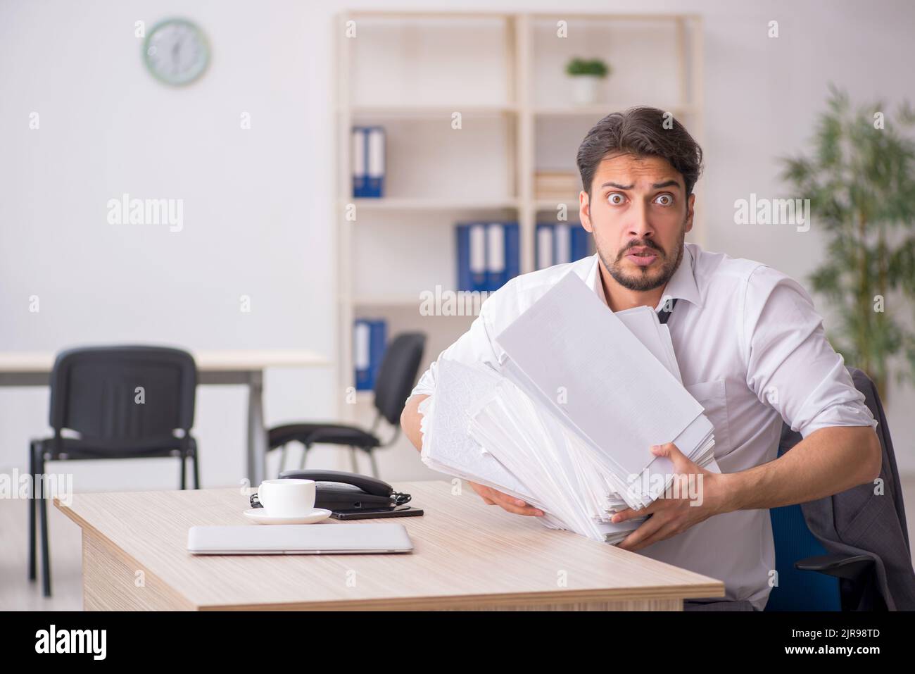 Young male employee and too much work at workplace Stock Photo - Alamy